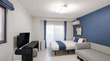 Quarto de hotel moderno com cama, sofá, escrivaninha e televisão, além de janela com cortinas.