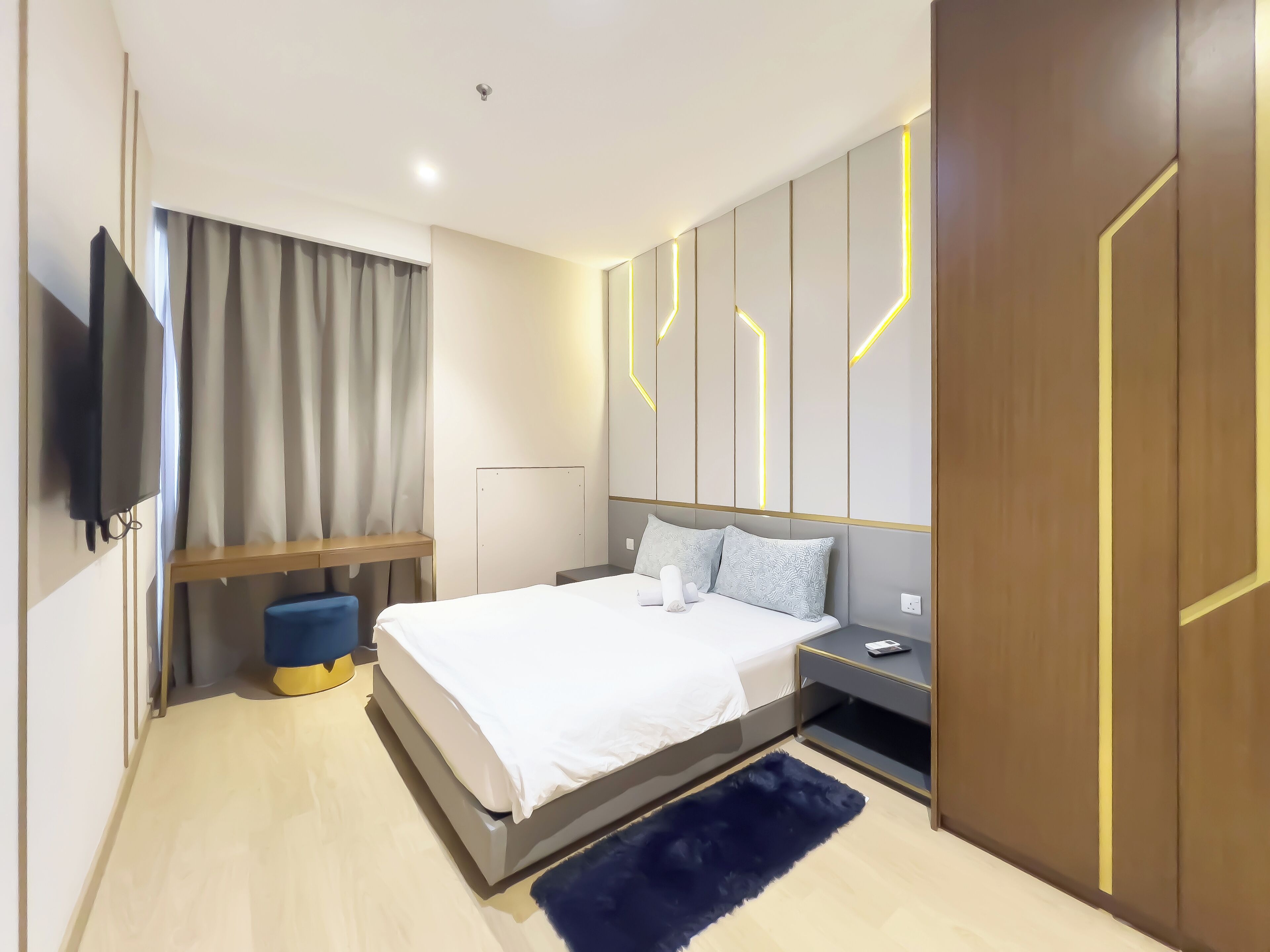 Quarto de hotel moderno com uma cama grande, uma televisão de tela plana na parede, uma mesinha de cabeceira de madeira e um guarda-roupa.