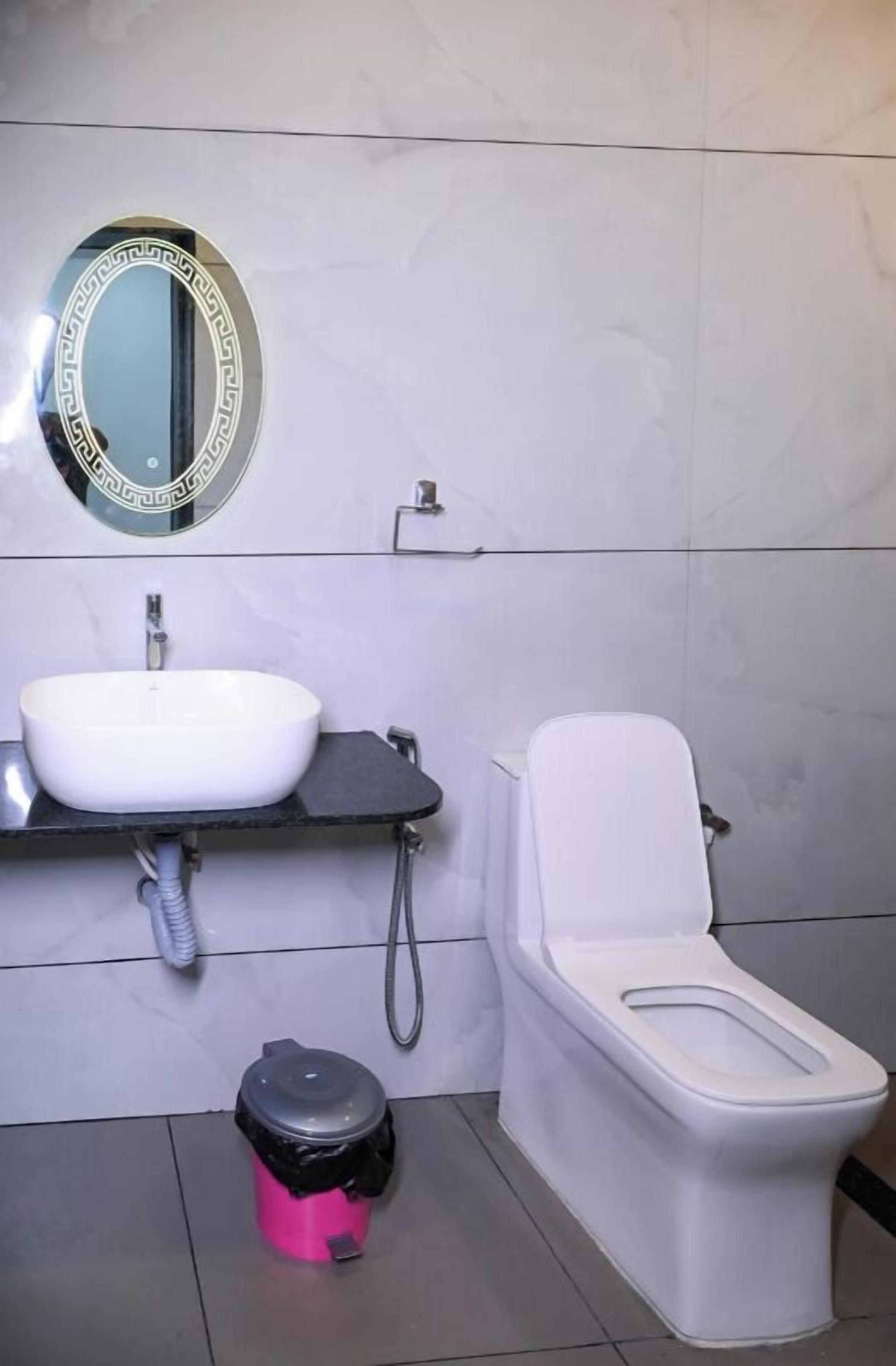 Casa de banho com lavatório branco, sanita e um contentor de lixo.