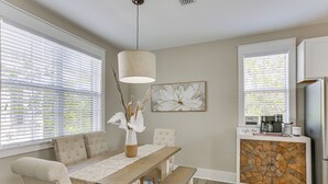 Uma área de refeições com uma mesa de madeira, cadeiras acolchoadas, um vaso com plantas secas e uma grande pintura de flores na parede.