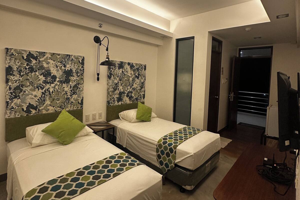 Quarto de hotel com duas camas, uma escrivaninha e uma televisão.