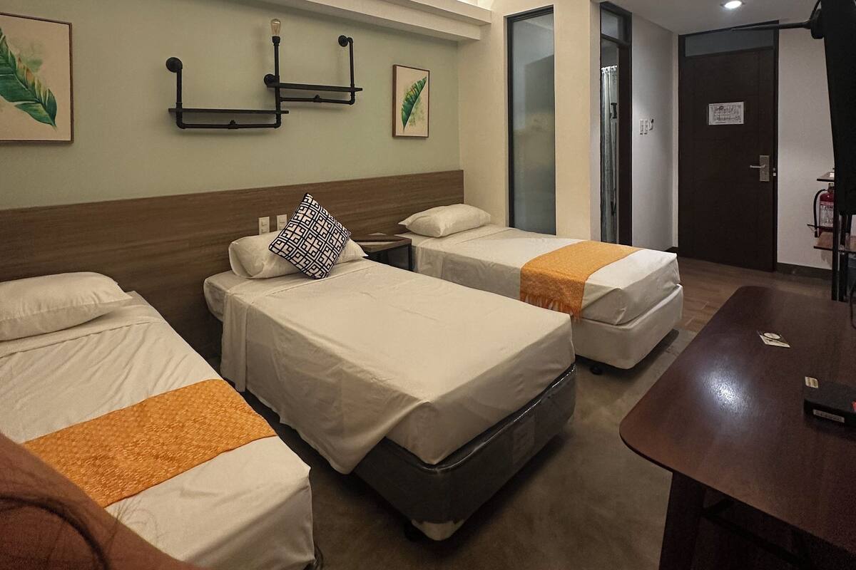 Quarto de hotel com três camas, uma mesa e uma televisão.