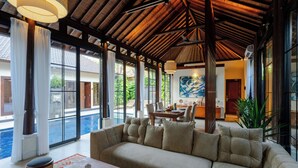 Uma sala ampla com um sofá grande, uma mesa de jantar e vista para uma piscina.