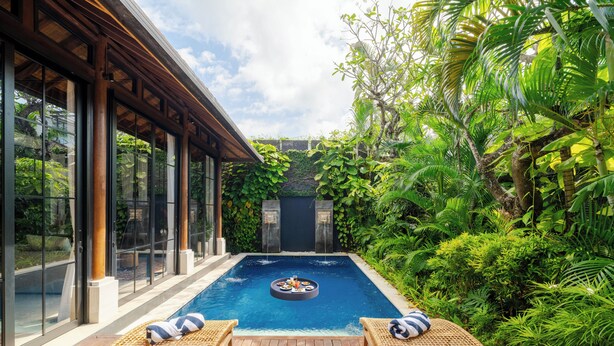 Piscina com espreguiçadeiras e bar flutuante, cercada por vegetação exuberante.