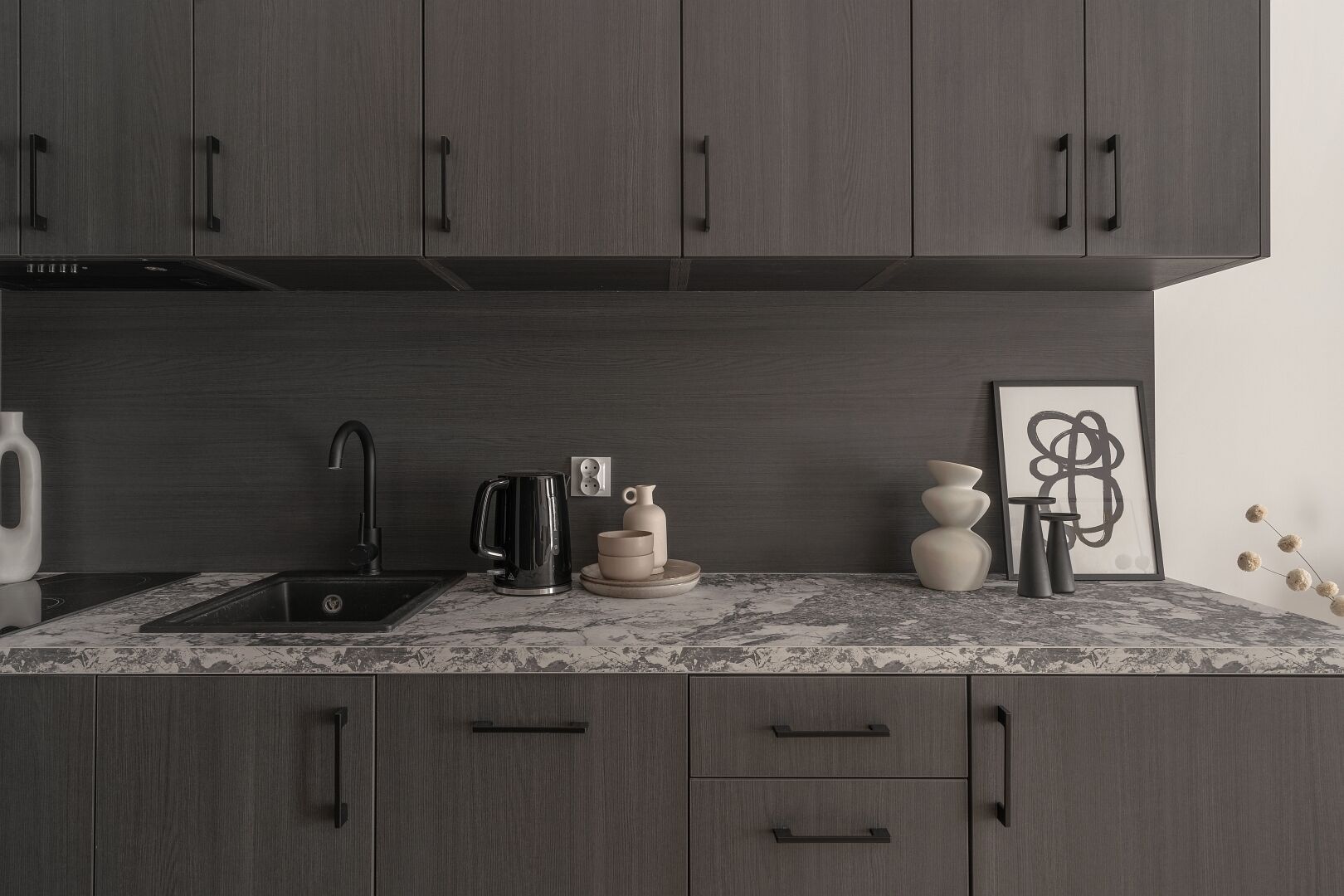 Uma cozinha moderna com armários de madeira escura, uma torneira preta, uma cafeteira e objetos decorativos na bancada.