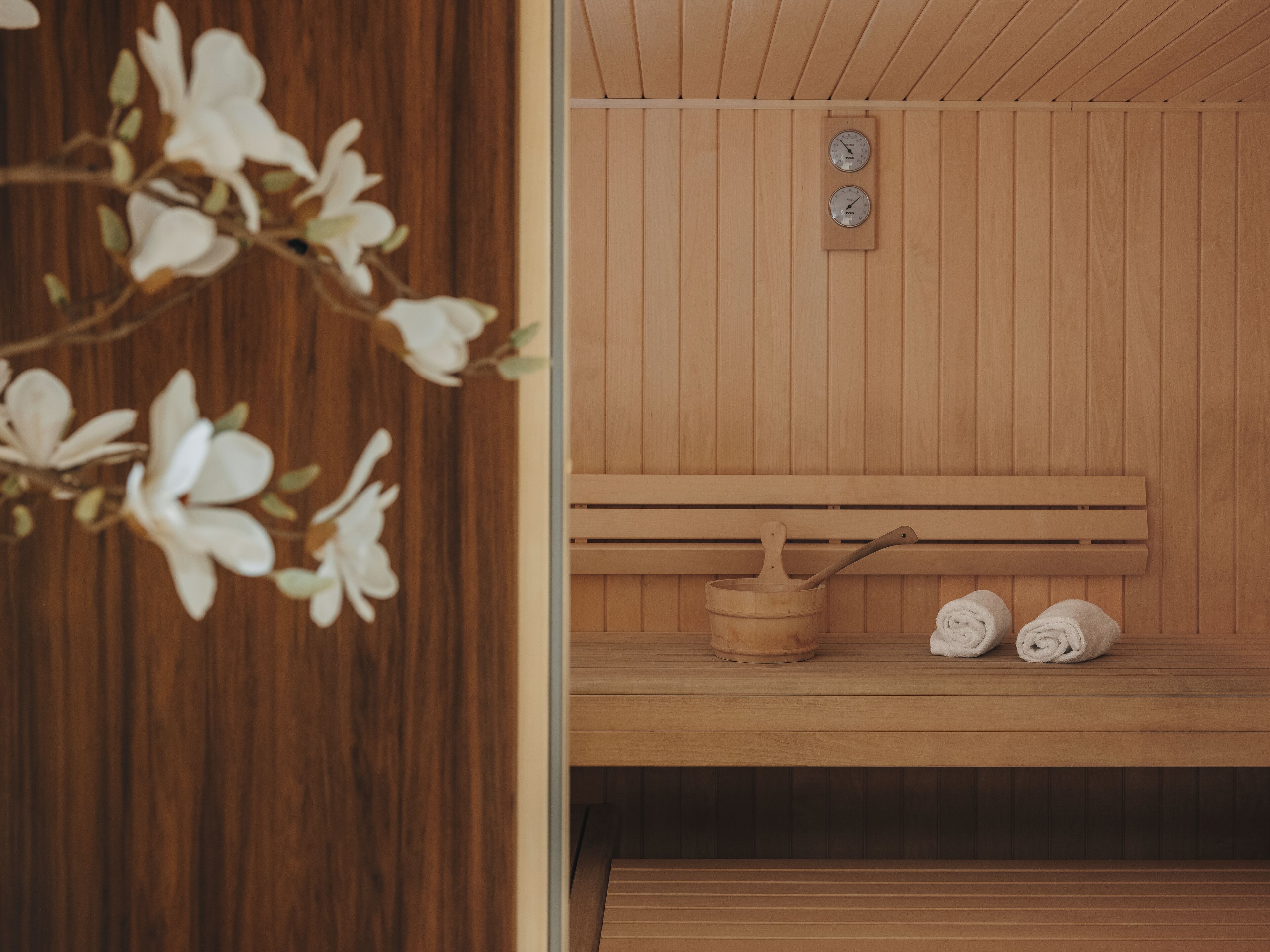 Uma sauna de madeira com um banco, um balde de madeira e duas toalhas enroladas.