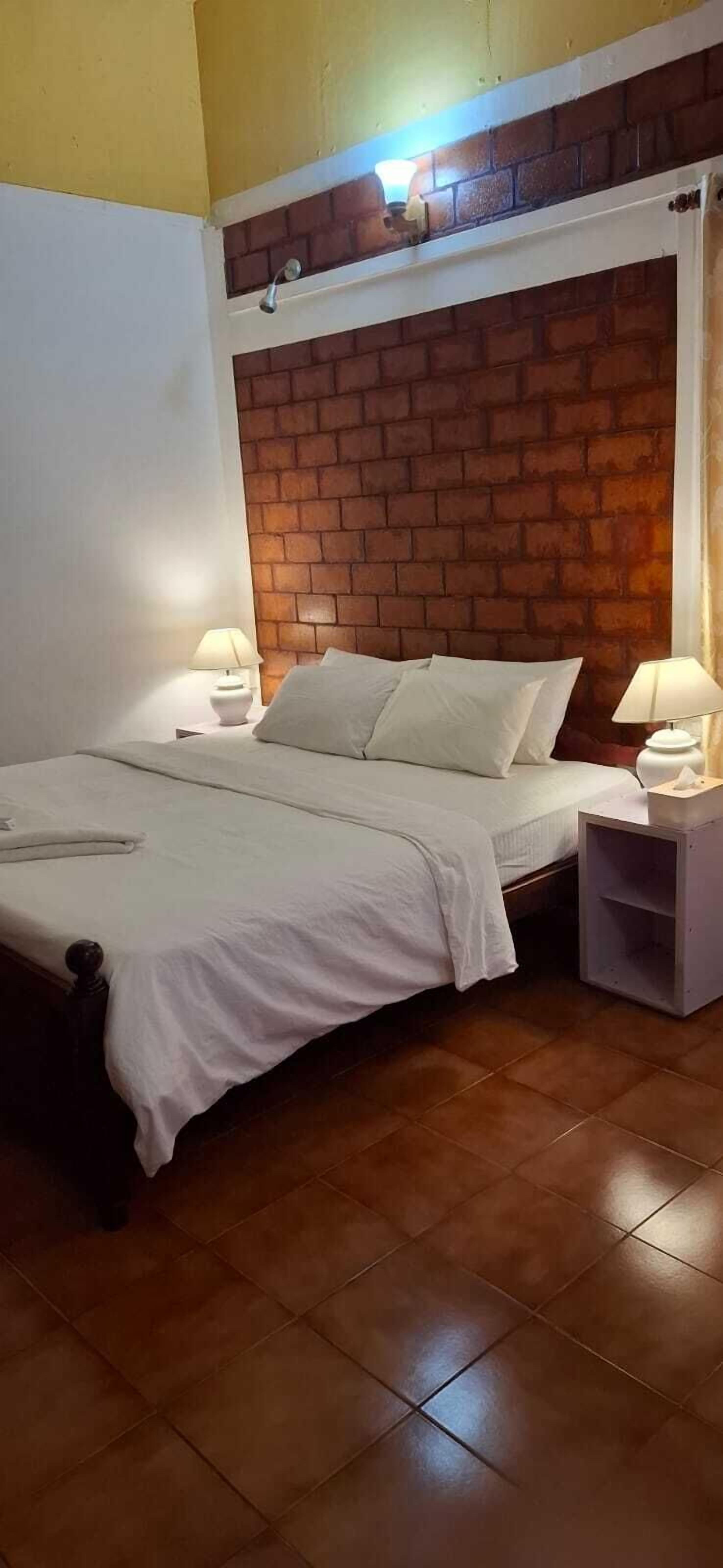 Uma cama de solteiro com roupa de cama branca, uma parede de tijolos decorativa e duas luminárias de cabeceira.