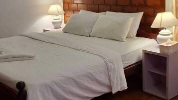Uma cama de solteiro com roupa de cama branca, uma parede de tijolos decorativa e duas luminárias de cabeceira.