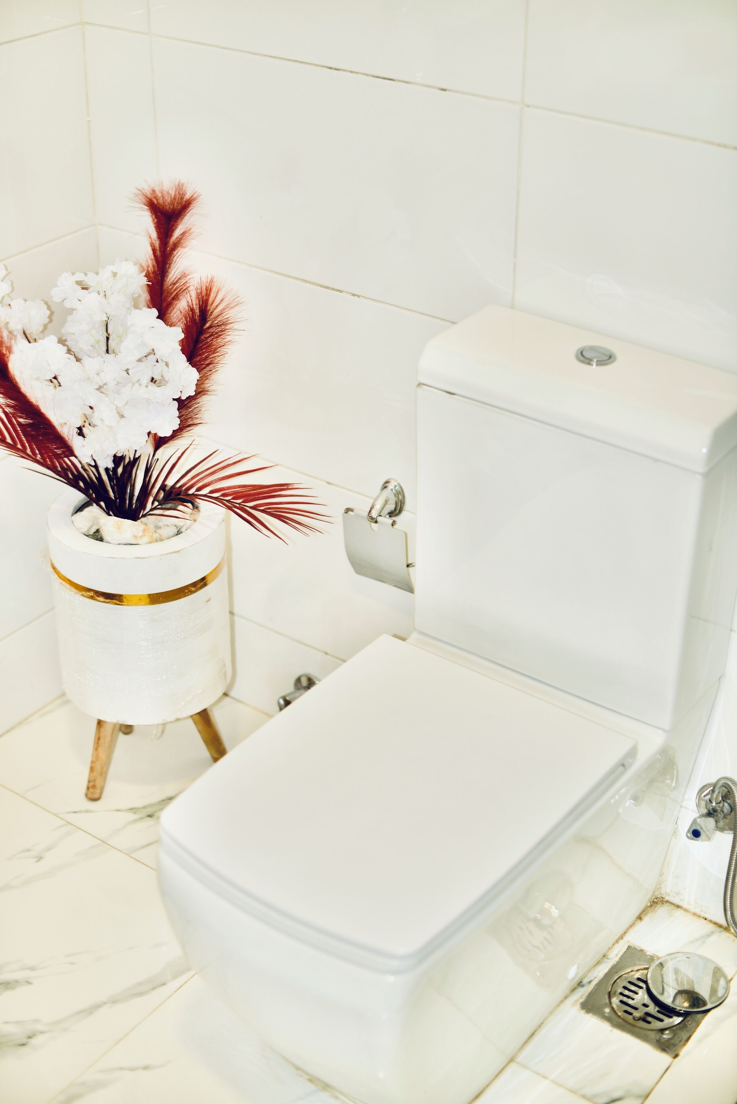 Casa de banho com sanita, soalho em mármore e um pequeno vaso de flores branco sobre um pedestal.
