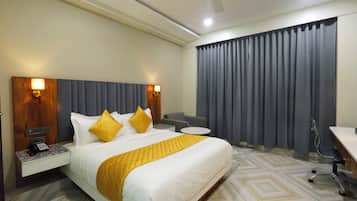 Quarto de hotel com uma cama grande, mesas de cabeceira, escrivaninha, cadeira e cortina.
