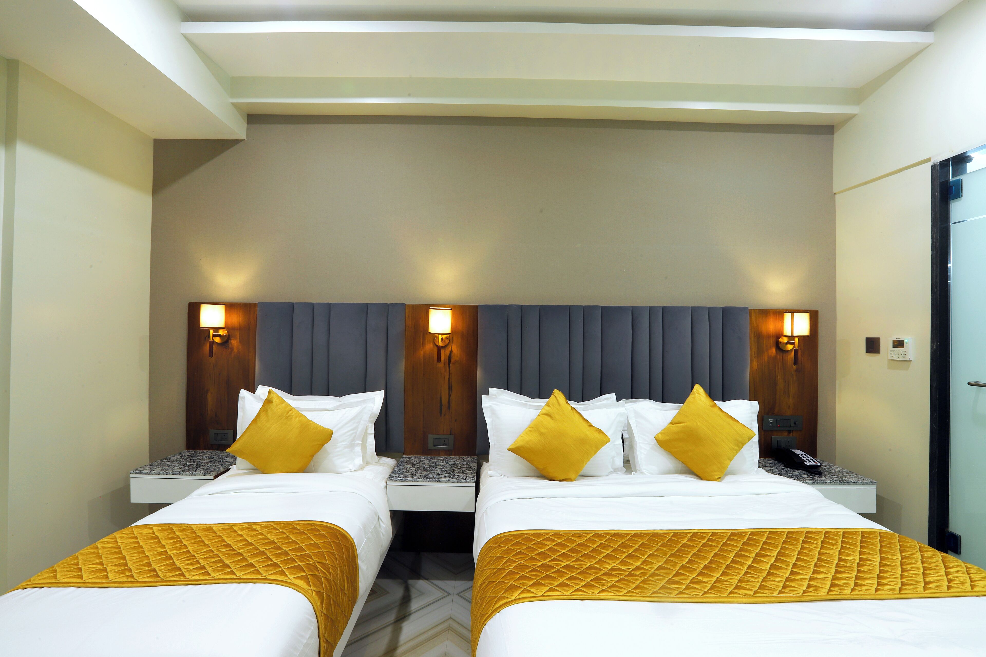 Quarto de hotel com duas camas, cada uma com cabeceira, mesas de cabeceira e luminárias.