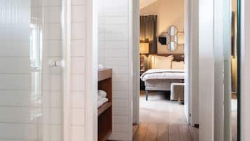 Quarto de hotel com cama, mesa de cabeceira, luminária e vista para o corredor.