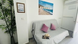 Um quarto com uma cama, um cartaz de uma praia, uma planta em vaso e uma porta.