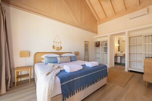 Quarto com cama, mesas de cabeceira, guarda-roupa e banheiro visível por uma porta aberta.