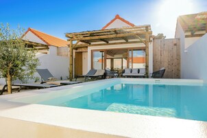 Piscina com espreguiçadeiras, pergolado e cerca de madeira.