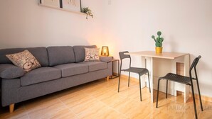 Uma sala de estar moderna com um sofá cinzento, duas cadeiras pretas, uma pequena mesa com um cacto e quadros na parede.