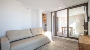 Uma sala de estar moderna com um sofá bege, um armário de madeira e uma porta de vidro deslizante que dá para uma área de jantar.