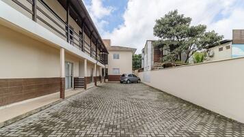 Pátio pavimentado com um carro estacionado ao fundo, rodeado por edifícios com varandas e uma árvore.