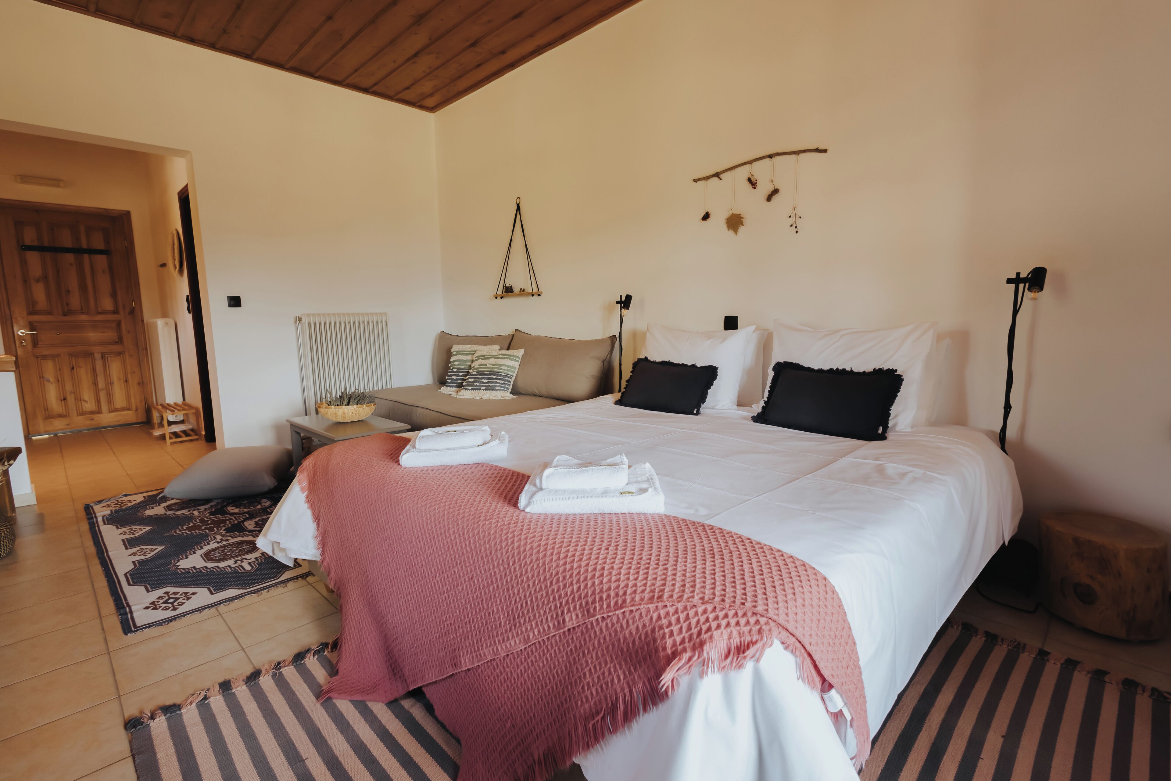 Quarto com cama, almofadas, mesa de cabeceira, abajur, radiador, porta de madeira e tapete.