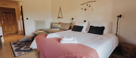 Quarto com cama, almofadas, mesa de cabeceira, abajur, radiador, porta de madeira e tapete.