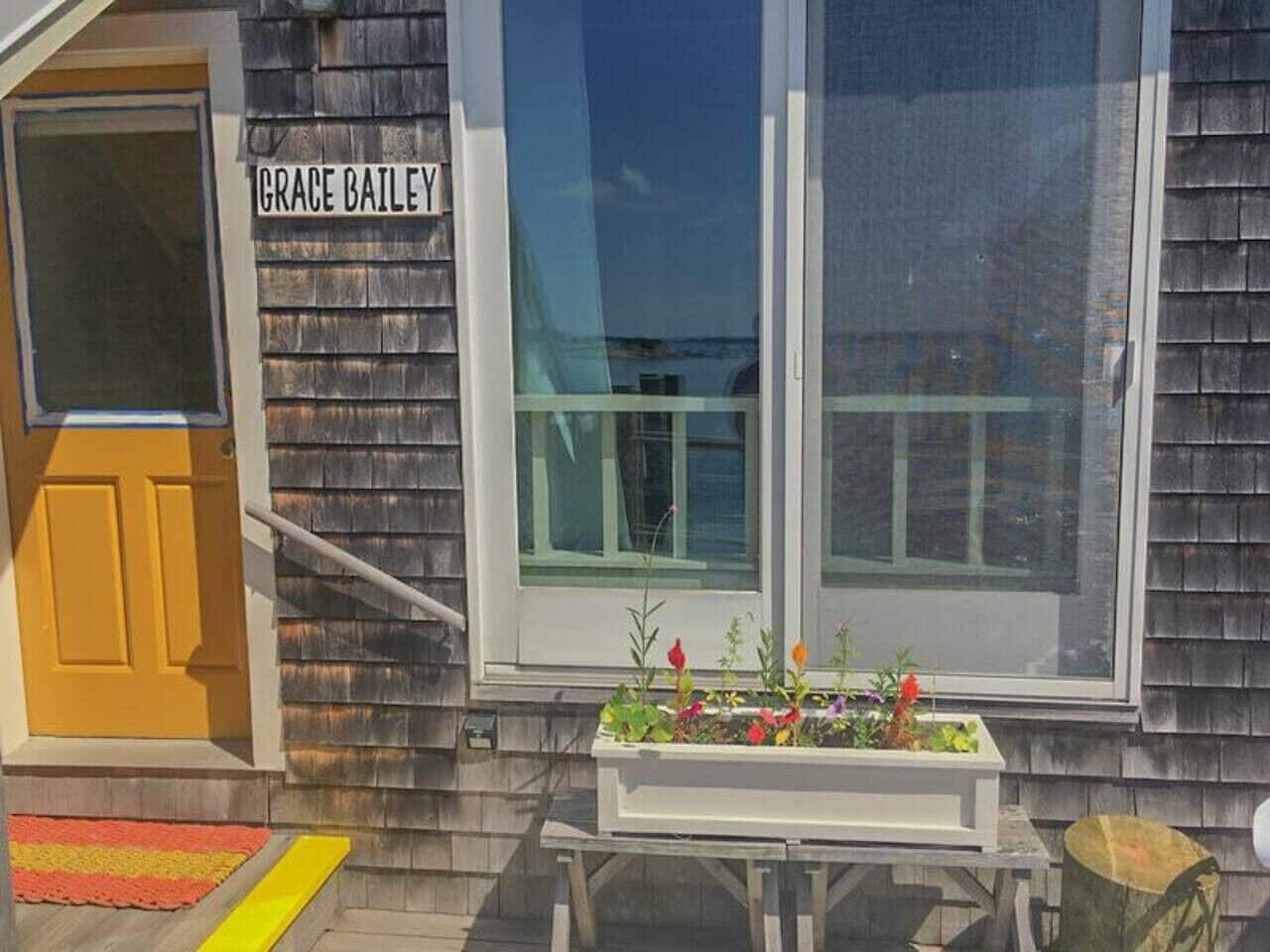 Uma casa com uma porta amarela e uma placa com o texto 'GRACE BAILEY'.