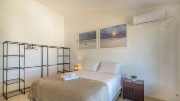 Quarto com cama, guarda-roupa de metal, mesa de cabeceira com abajur e ar-condicionado fixado na parede.