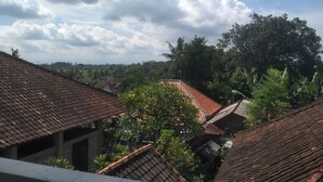 Vista de edifícios tradicionais com telhados de azulejos, rodeados por vegetação exuberante e um céu parcialmente nublado.