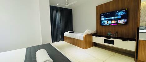 Quarto de hotel moderno com uma cama, televisão presa na parede, uma pequena mesa de cabeceira e um armário de madeira.