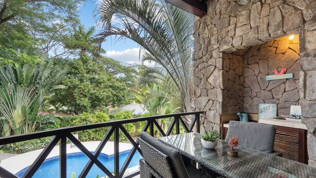 Área de piscina com mobiliário de vime, parede de pedra e vegetação exuberante.