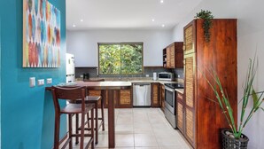 Uma cozinha moderna com armários de madeira, uma ilha central e uma janela ampla que oferece vista para o verde.