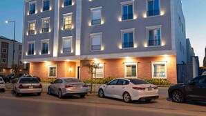 Um hotel com vários andares, fachada moderna, várias varandas e um estacionamento com diversos carros.