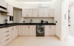 Cozinha moderna com armários de madeira clara, máquina de lavar embutida e bancada preta.