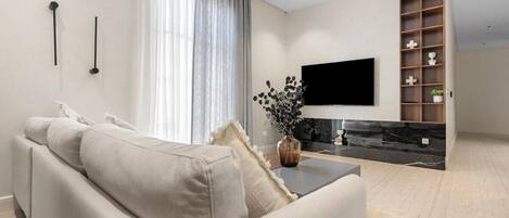 Uma sala de estar moderna com um sofá bege, uma televisão de tela plana fixada na parede, uma lareira de mármore e uma estante de madeira.