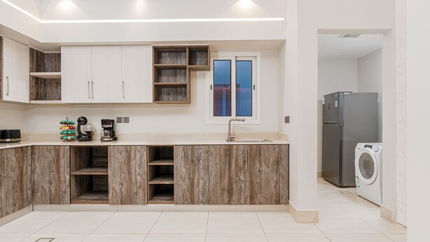 Cozinha moderna com armários de madeira, forno embutido, cafeteira e máquina de lavar.