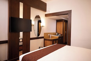 Quarto de hotel com cama, televisão na parede, espelho, pia e um armário de madeira.
