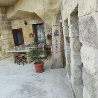 Um edifício de pedra com uma mesa, cadeiras, um vaso de planta e uma placa de madeira com a inscrição 'TOPRAK EARTH'.