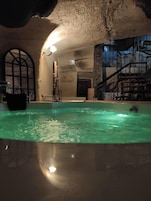 Piscina interna com parede de pedra e janela em arco.