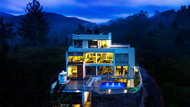 Uma casa moderna de dois andares com piscina, rodeada por uma paisagem montanhosa.