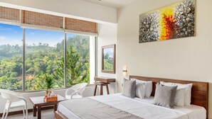 Quarto de hotel com uma janela grande, uma cama, uma escrivaninha, uma cadeira e um quadro na parede.