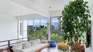 Uma sala de estar moderna com sofá, cadeiras de saco e uma grande janela com vista para áreas verdes e edifícios.