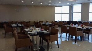 Uma ampla sala de jantar com várias mesas e cadeiras, grandes janelas que oferecem luz natural e um design moderno e limpo.
