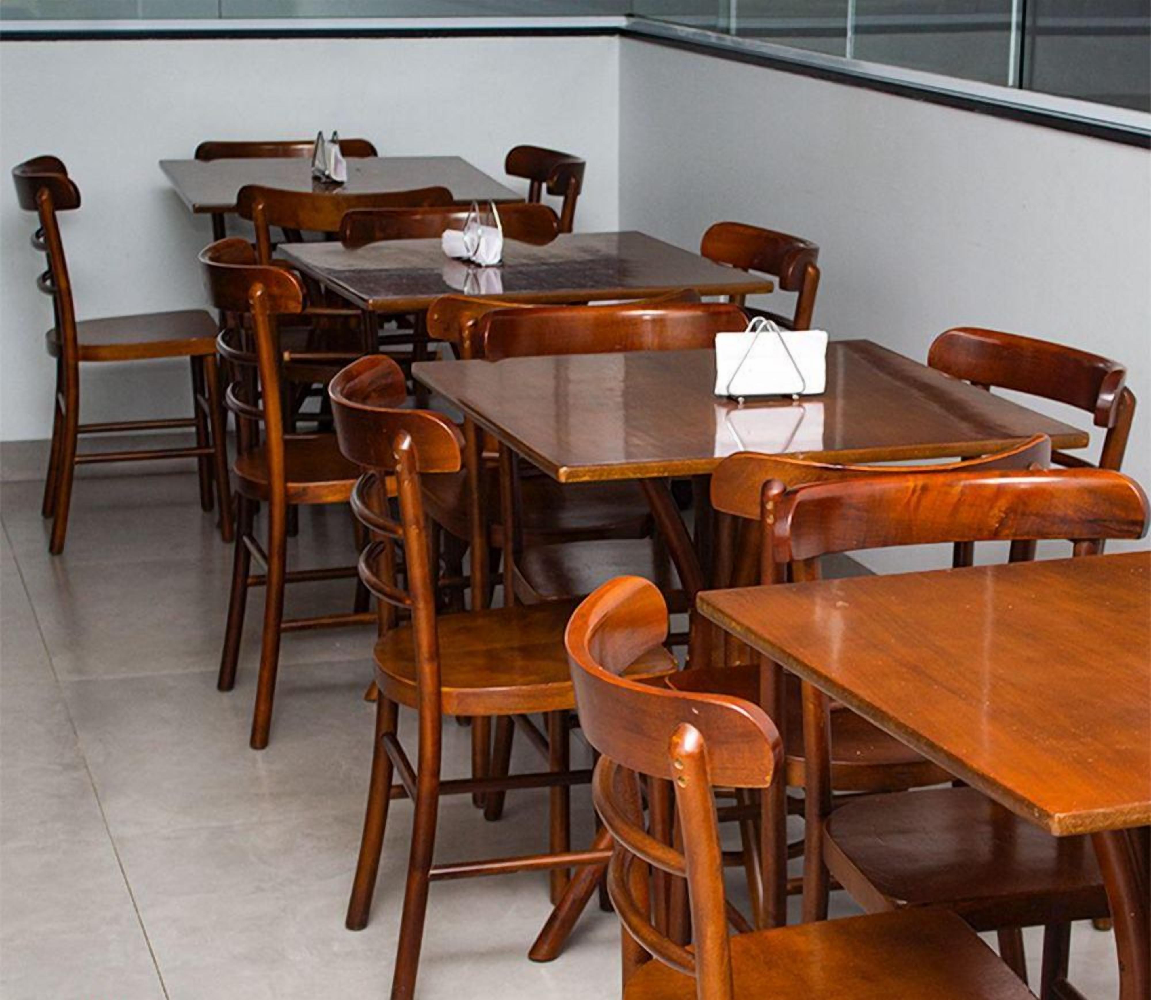 Uma área de jantar de hotel com mesas e cadeiras de madeira, uma bolsa branca em uma mesa e o logotipo do Hotel CBN no canto inferior esquerdo.