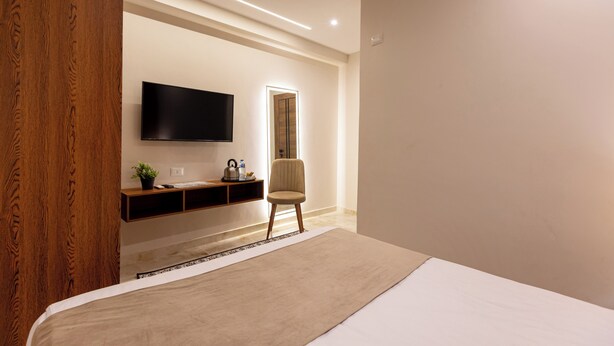 Um quarto moderno com uma cama, uma televisão fixada na parede, uma cadeira e um painel de madeira.