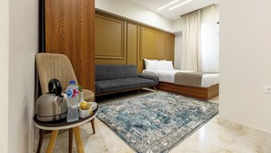 Quarto de hotel com cama, sofá, um pilar de madeira, uma mesinha com chaleira, garrafa de água e bandeja com limão.