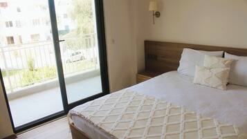 Quarto de hotel com uma cama, mesa de cabeceira, luminária e vista para a varanda externa.