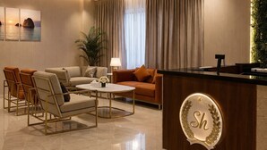 Um lobby moderno de hotel com balcão de recepção, área de estar e uma grande janela com cortinas.