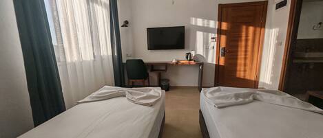 Quarto de hotel com duas camas de solteiro, uma escrivaninha com cadeira, uma televisão e uma porta de madeira.