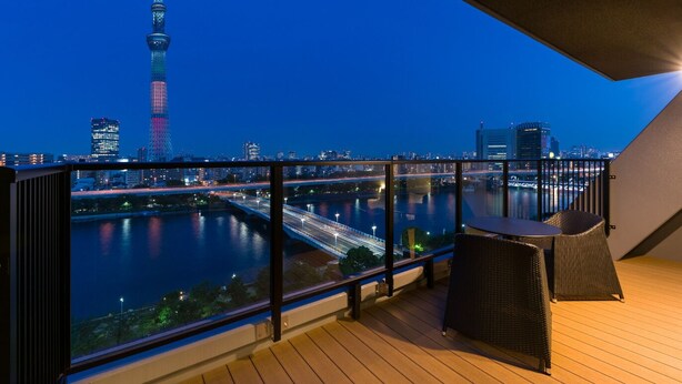 Uma varanda com vista para o horizonte urbano, incluindo uma torre imponente, ao entardecer.