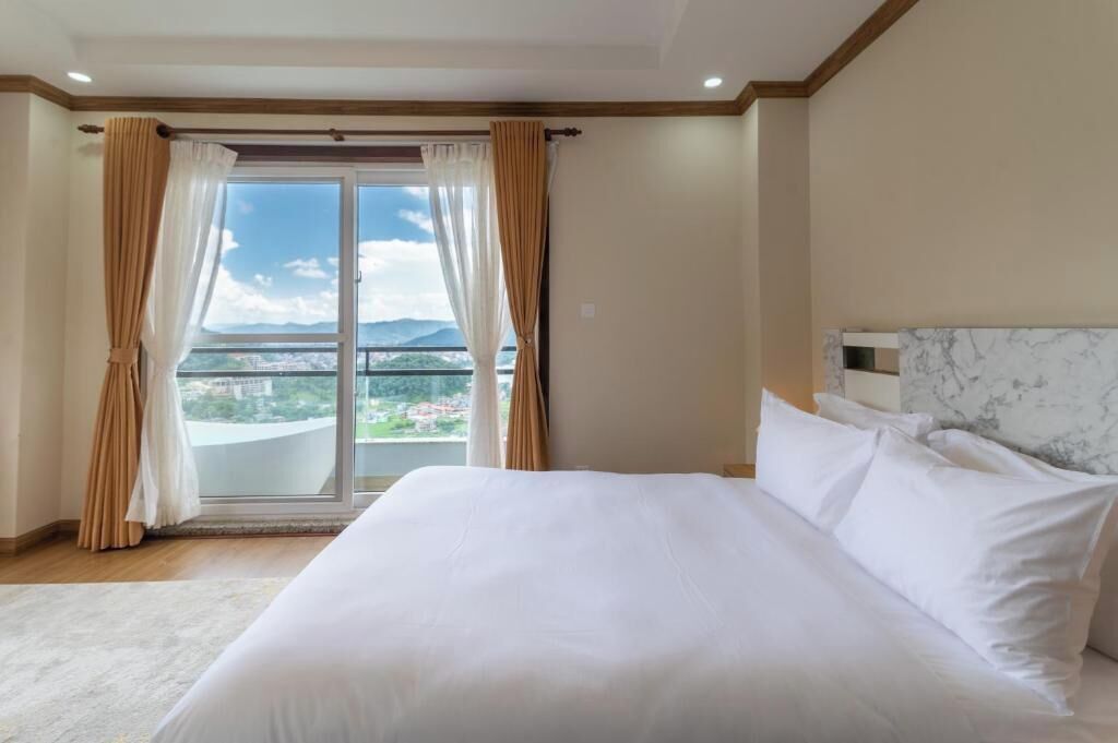 Quarto de hotel com uma cama grande, cabeceira de mármore e varanda com cortinas.
