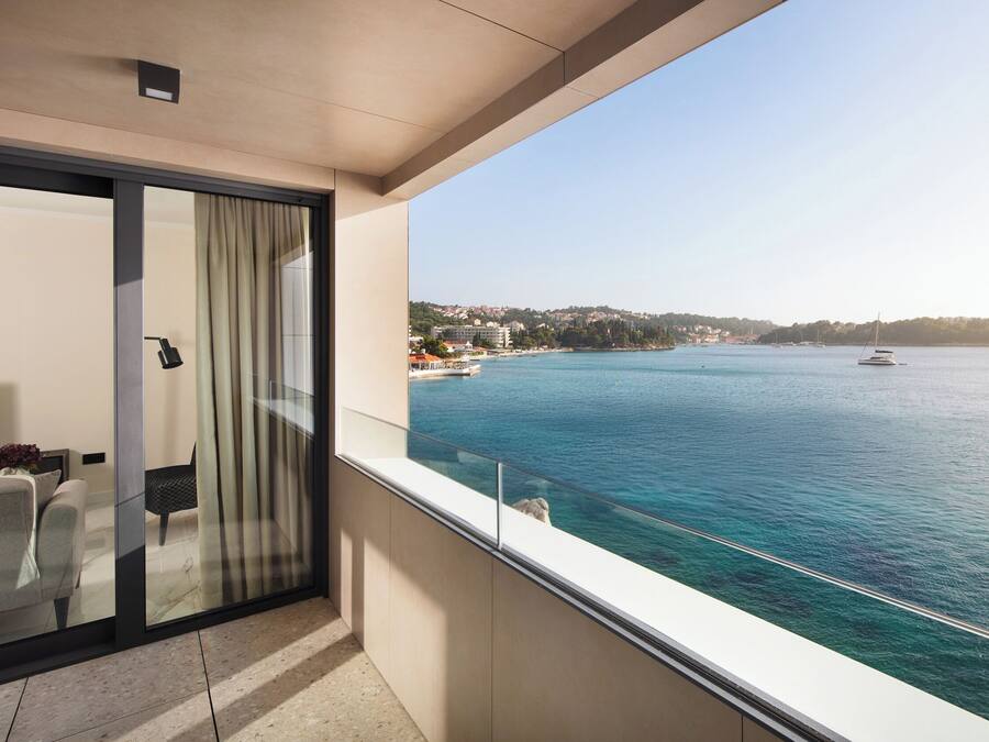 Uma varanda com vista desobstruída para o mar, uma cadeira, uma mesa e uma televisão.